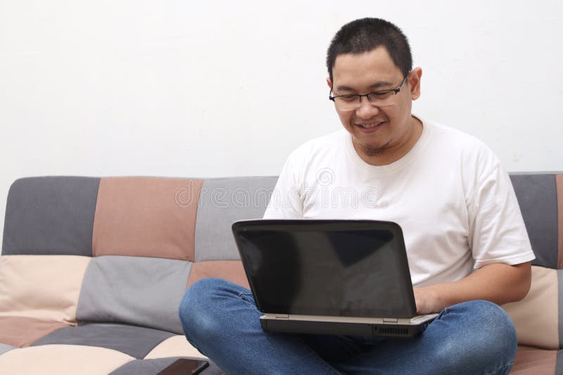 Cheerful Asian Man Using Computer and Smiling while Sitting on the Sofa ...