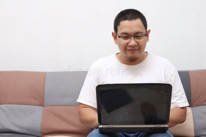 Cheerful Asian Man Using Computer and Smiling while Sitting on the Sofa ...