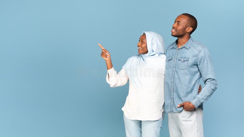 Cheerful Black Muslim Couple Pointing Finger Aside Over Blue Background ...