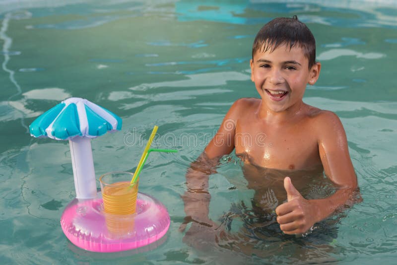 Cheerful Boy Bathes in the Pool with a Yellow Drink, Laughs, Thumbs Up ... Cheerful Boy Bathes in the Pool with a Yellow Drink, Laughs, Thumbs Up ...