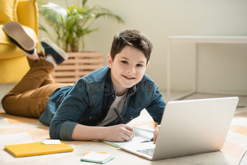 Boy Lying on Floor, Writing in Copy Book and Using Laptop while Smiling ...