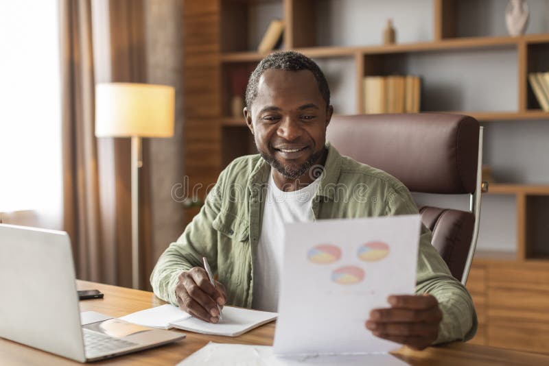 Cheerful Busy Middle Aged Black Guy Makes Notes and Works with Graphs ...