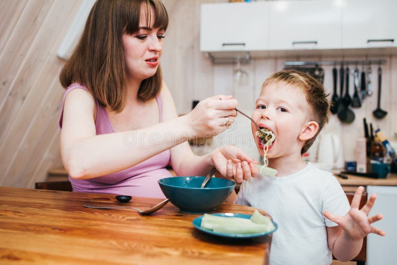 Cheerful Child Eating Pasta in the Kitchen with Mom Stock Photo - Image ...