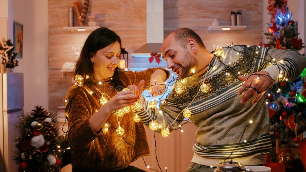 Cheerful Couple Getting Tangled in String of Twinkle Lights Stock Photo ...