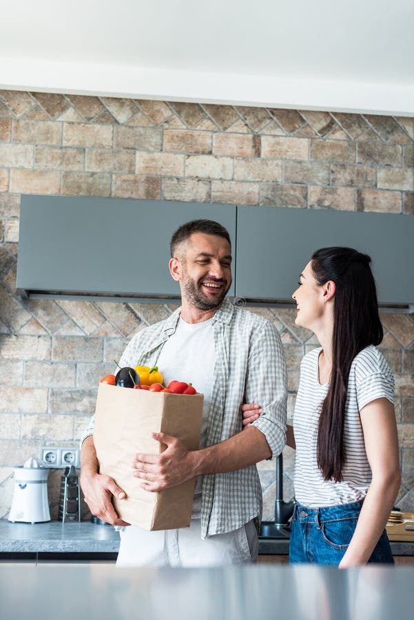 Cheerful Couple with Paper Package Full of Fresh Vegetables Standing in ...