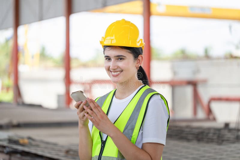 Cheerful Female Engineer in the Hard Hat Uses Mobile Phone, Industrial Worker Using Mobile ...