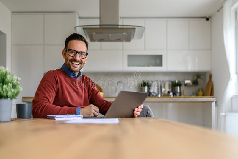 Cheerful Handsome Man with Laptop and Note Pad on Desk Working from ...