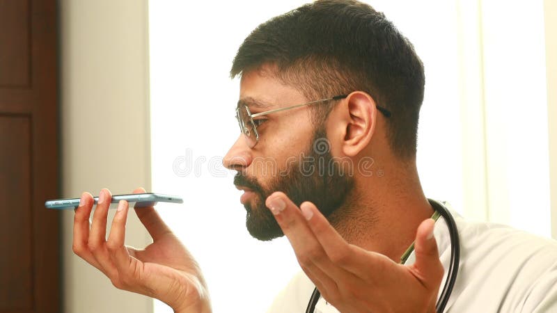 Cheerful Indian Doctor Recording a Voice Message on Mobile Phone in ... Cheerful Indian Doctor Recording a Voice Message on Mobile Phone in ...
