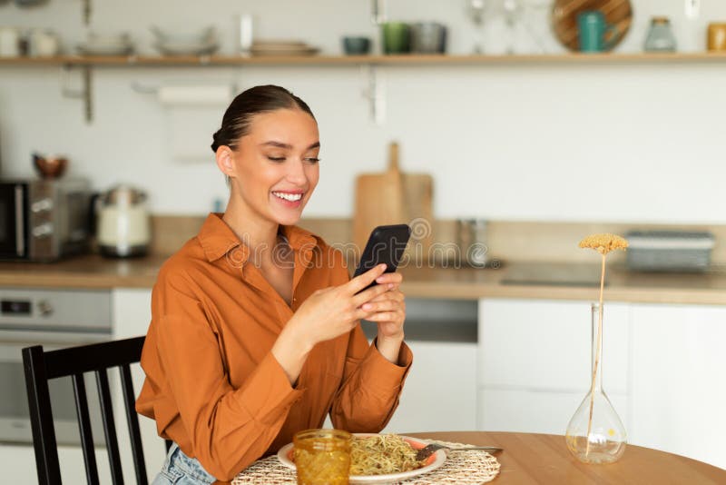 Cheerful Lady Using Smartphone while Sitting at Kitchen Table and ...