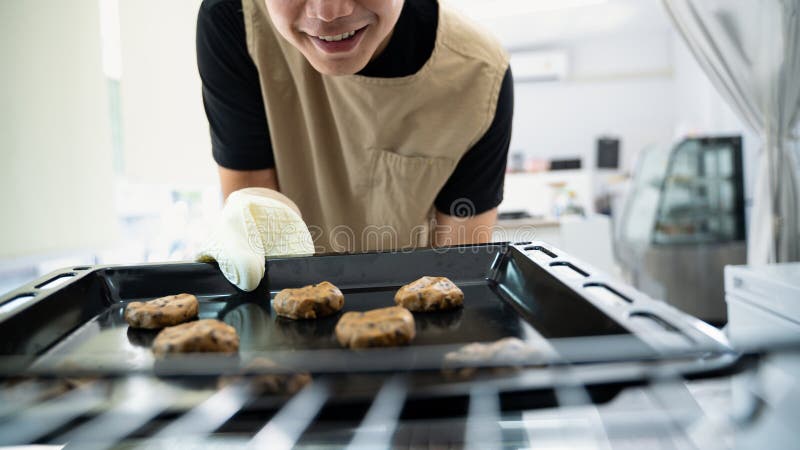 Cheerful Male Baker a Tray of Chocolate Chip Cookie Dough into the Oven ...