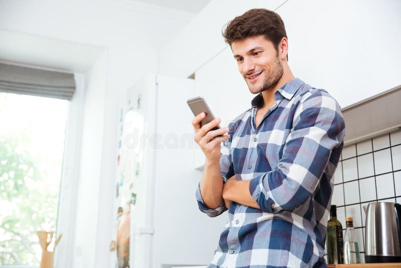 Cheerful Man Standing and Using Mobile Phone on the Kitchen Stock Image ...