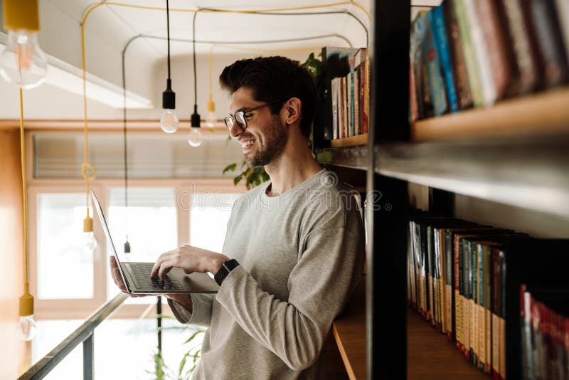 Cheerful Man Using Laptop Computer while Standing in Library Stock ...