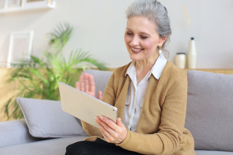 Cheerful Middle Aged Woman Sitting on Sofa, Using Computer Tablet Apps ...