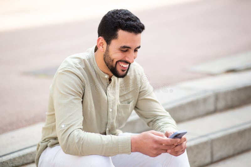 Cheerful Middle Eastern Man Sitting Outside and Using Cell Phone Stock ...
