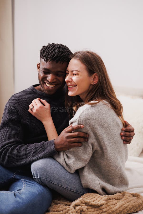 Cheerful Multiethnic Couple Cuddling while Sitting on Bed at Home Stock ...