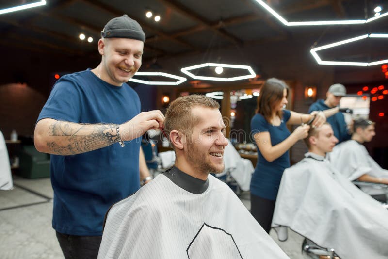 Cheerful Professional Tattooed Barber Making Haircut for a Young and ... Cheerful Professional Tattooed Barber Making Haircut for a Young and ...