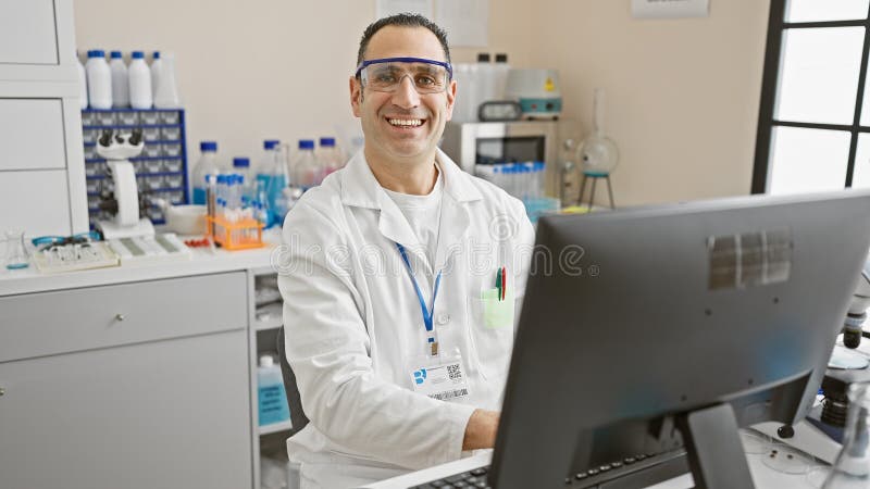 A Cheerful Scientist Man in a Lab Coat Works at a Computer in a Bright ...