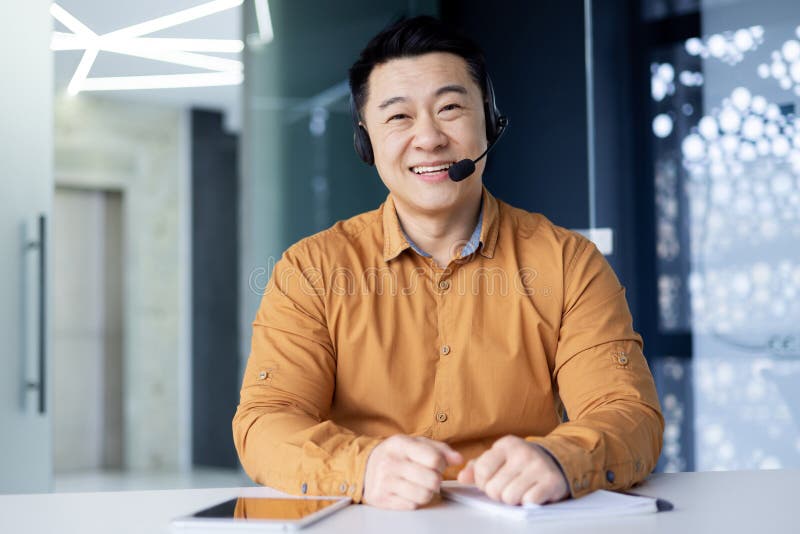 Asian Smiling Young Man Sitting in Office at Desk in Front of Camera ...