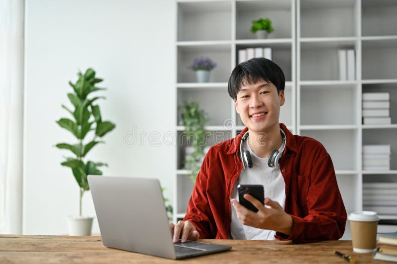 Cheerful Young College Student Using Laptop and Smartphone while Study ...