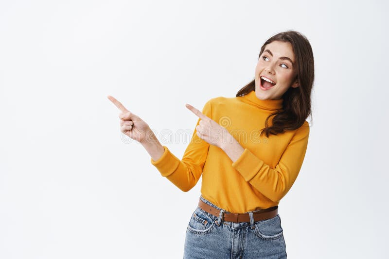 Cheerful Young Female Model Smiling Pointing Fingers Left At Logo With