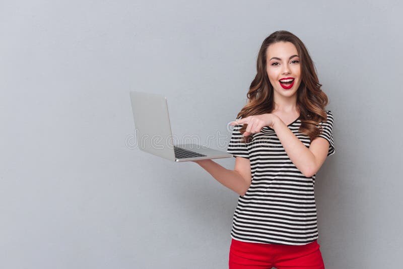 Cheerful Young Lady Standing Over Grey Wall and Using Laptop Stock ...