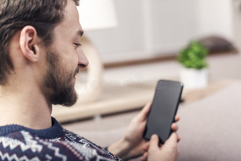 Cheerful Young Man Holding Mobile Phone and Smiling at Home. Stock ... Cheerful Young Man Holding Mobile Phone and Smiling at Home. Stock ...