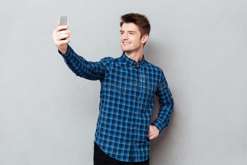 Cheerful Young Man Standing Over Grey Wall and Make Selfie Stock Image ...