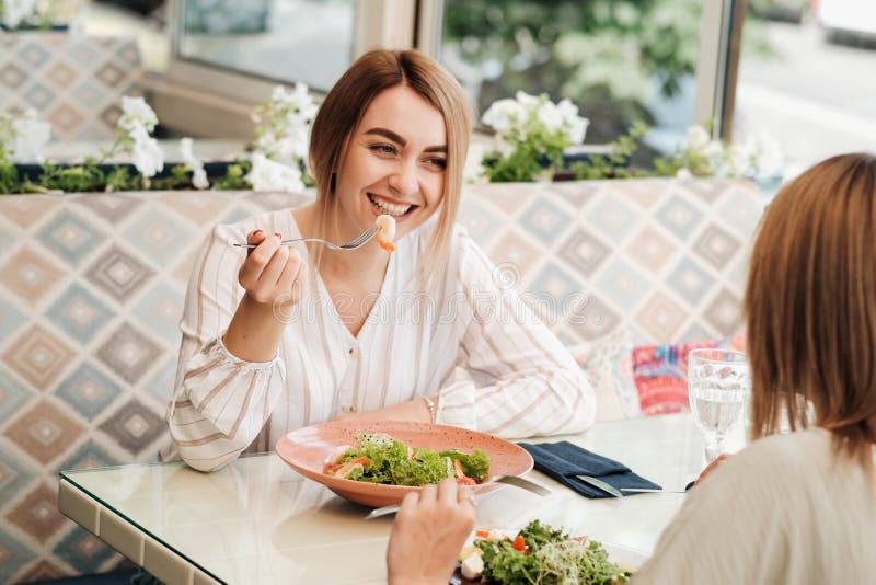 Cheerful Young Woman Having Lunch With Her Female Friend Eating Salad With Shrimp In The