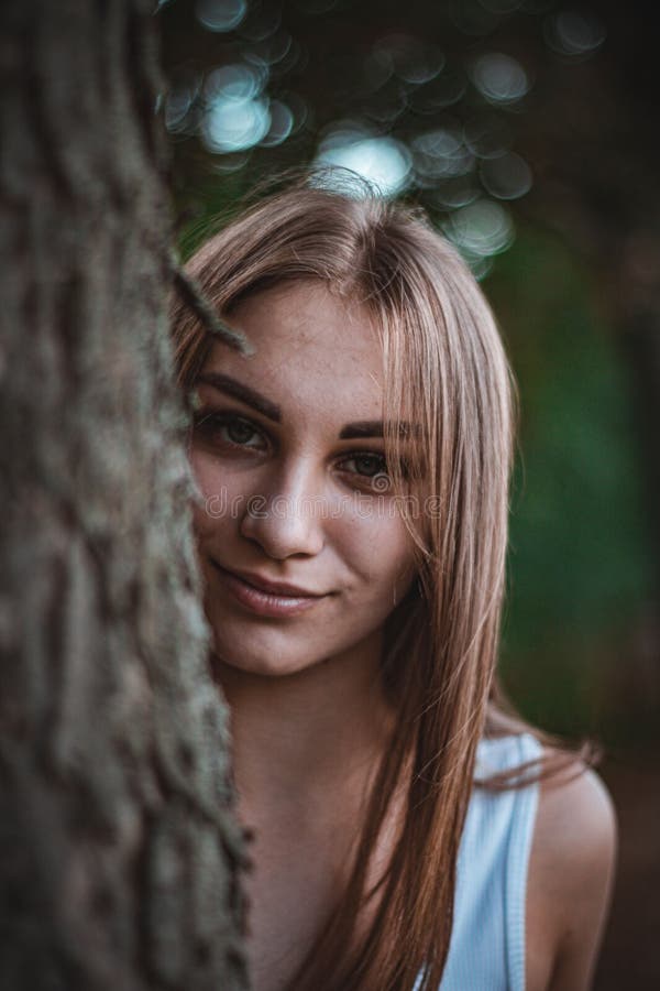 A Young Woman Smiles while Leaning on a Tree Trunk in the Forest Stock ...
