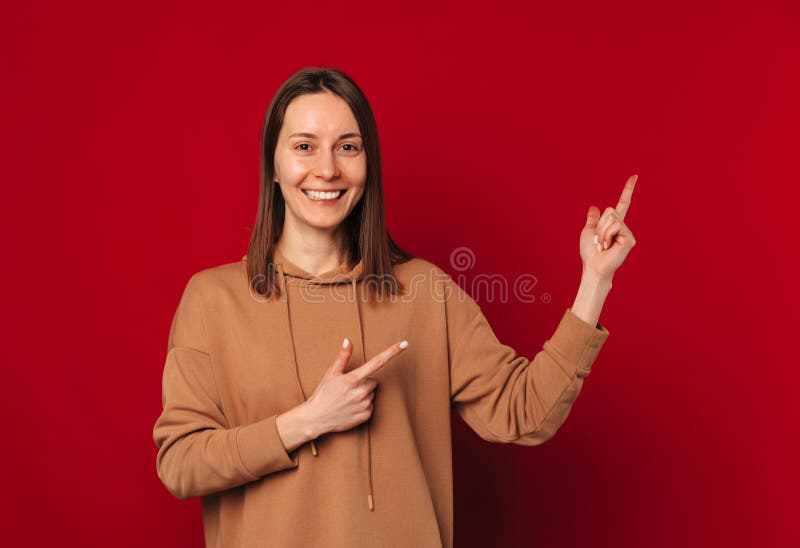 Cheerful Young Woman is Pointing Aside with Two Hands Over Red ...