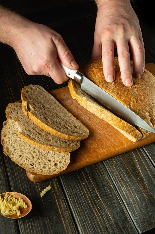 Chef Cuts Fresh Bread with a Knife on a Kitchen Board Close-up. Slicing ...