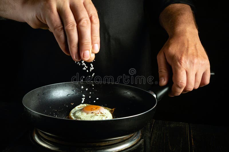 The Chef Fries an Egg in a Frying Pan. Adding Salt To the Eggs by the ...