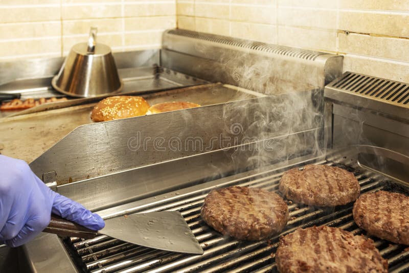 A Chef with a Gloved Hand Preparing Beef Burgers on a Grill Next To ...
