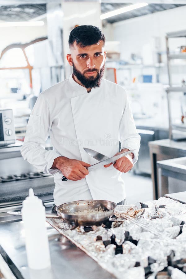 Chef in White Uniform Standing at Kitchen. Holding Knives in Hands ...