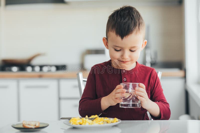 A Child in the Afternoon in a White Light Kitchen Drinks Water from a ...