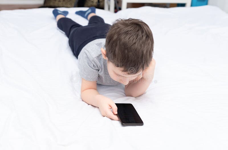 Child Boy Lying on the Bed with Smartphone Playing Games or Studying ...