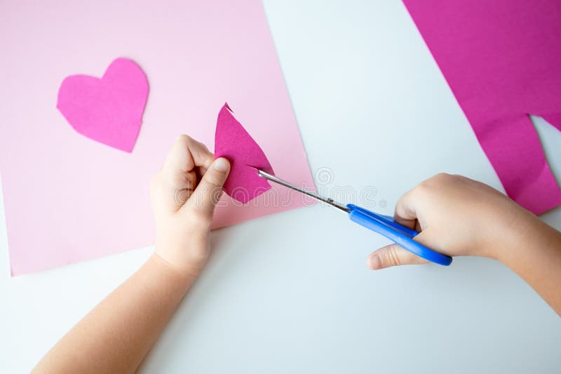 Child Cutting Pink Paper Heart with Scissors on White Table Stock Image ...
