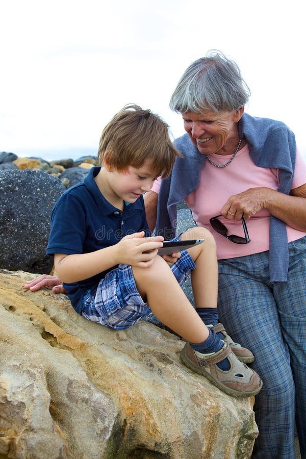 Grandma Kissing With Love Grandson Playing With Tablet On The Beach
