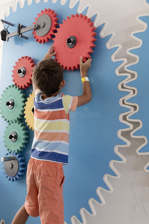 Child Interacting with Colorful Gears on a Mechanical Wall, Exploring ...