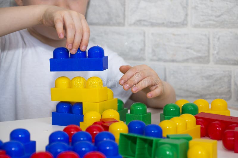 A Child in Light Clothes is Building a Tower from Large Plastic Blocks ...