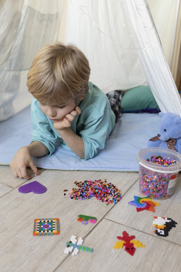 Child Makes Figures from Multi-colored Thermo Mosaics Lying on Floor in ...