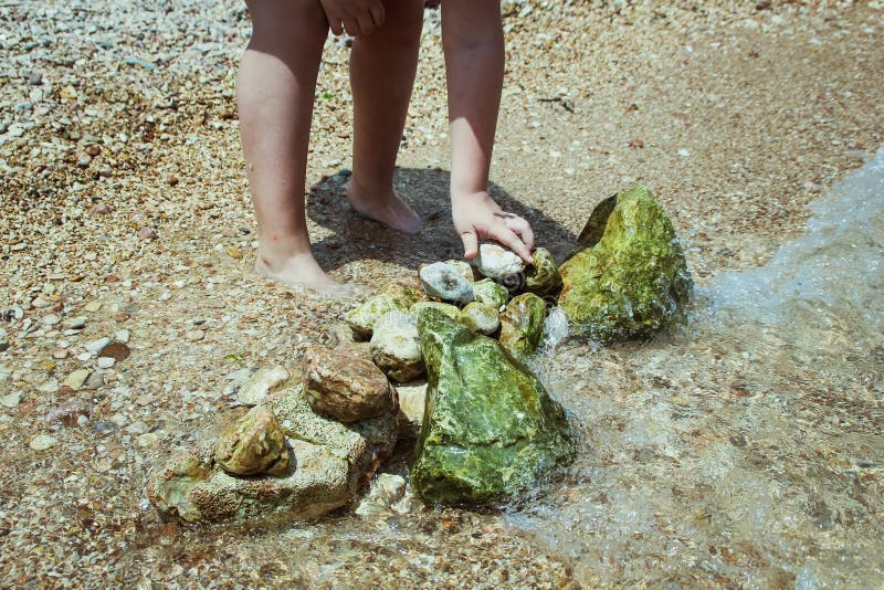 Child Playing on the Beach and Building Stone Tower. Stones on the ...