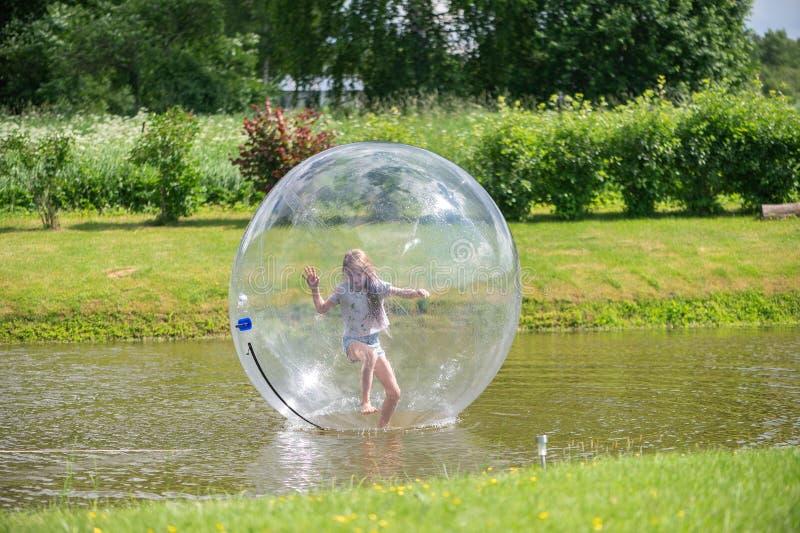 Child Playing Inside a Large Inflatable Ball on a Pond with Lush ...