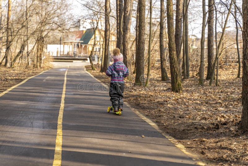 The Child Races on a Scooter Along an Asphalt Road through a Spring ...