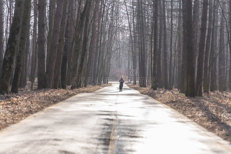 The Child Races on a Scooter Along an Asphalt Road through a Spring ...