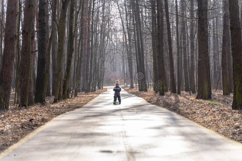 The Child Races on a Scooter Along an Asphalt Road through a Spring ...