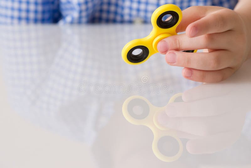 Child`s Hand Spinning a Fidget Spinner Device. Playing with a Yellow ...