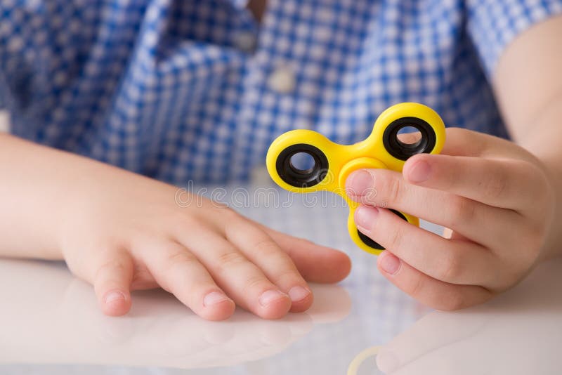 Child`s Hand Spinning a Fidget Spinner Device. Playing with a Yellow ...