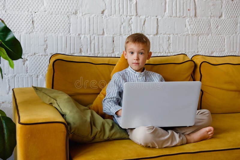 The Child is Sitting on a Yellow Sofa with a Laptop. the Boy Studies at ...