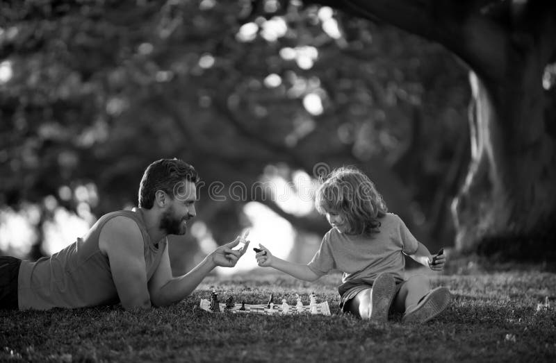 Child Son Laying on Grass and Playing Chess with Father. Stock Image ...